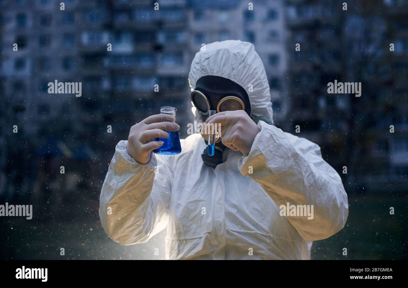 Scientist wearing a coverall and a gas mask, holding glass flasks with ...