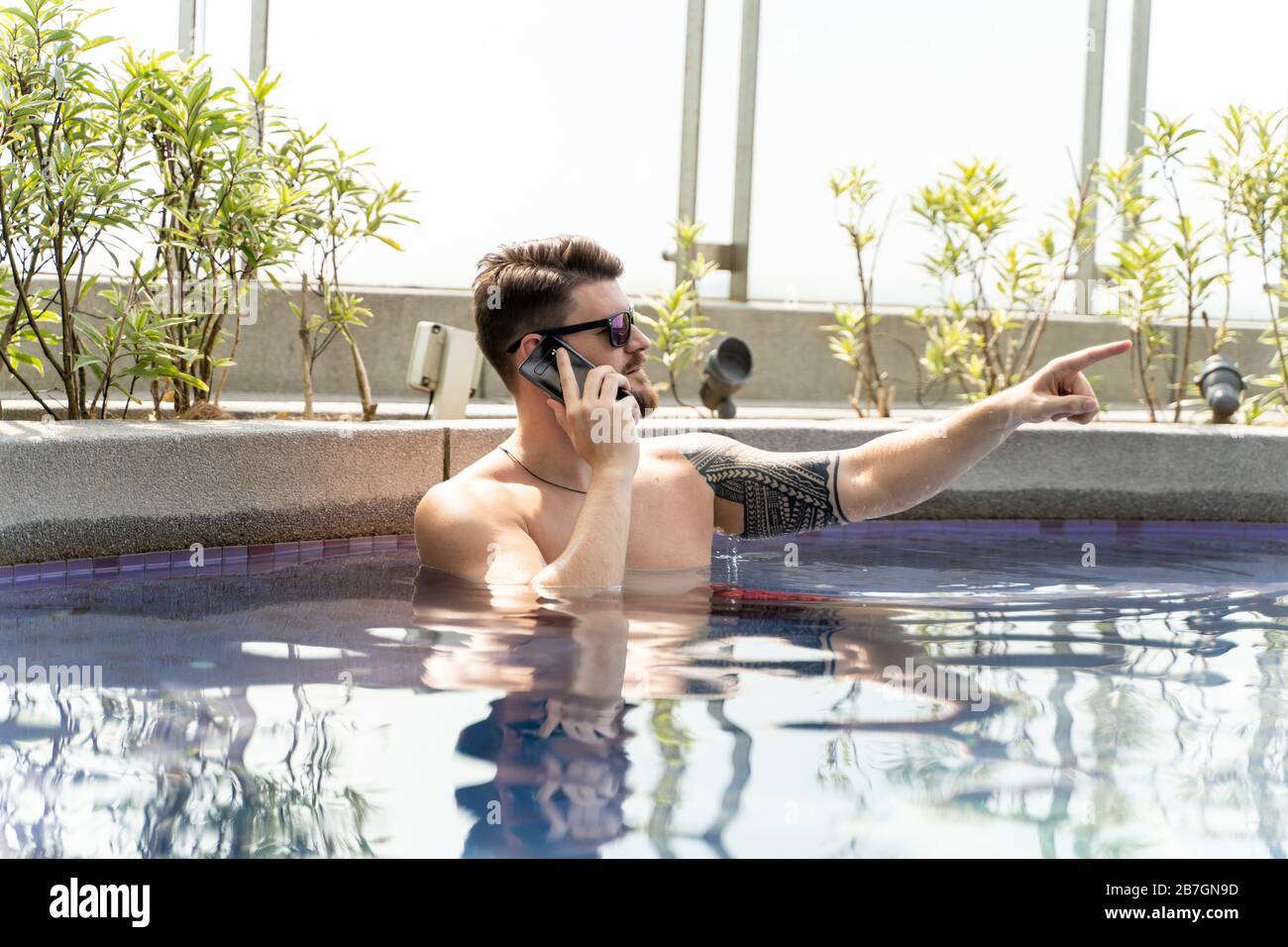 Young man with sunglasses using his cell phone inside a pool while ...