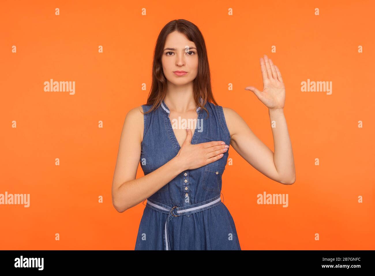 I swear! Dedicated honest brunette woman in denim dress standing with ...