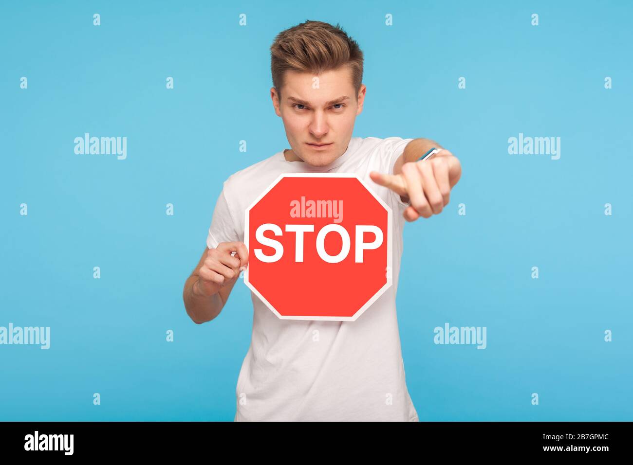 Portrait of young serious man in t-shirt holding red Stop sign and ...