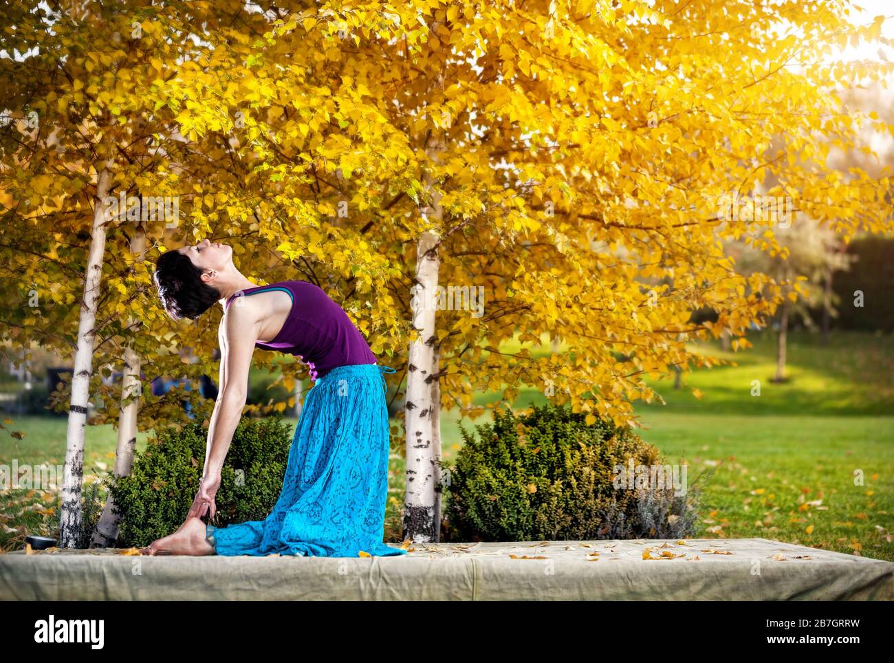 Young woman doing yoga in autumn city park near yellow birch trees ...