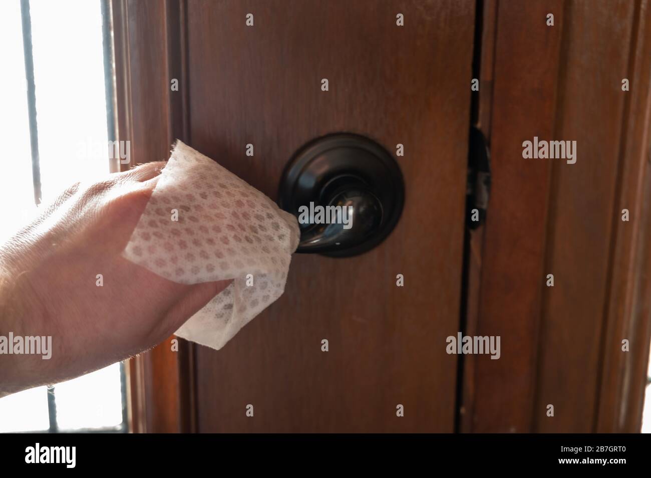 Caucasian hand holding a sanitized cleaning wipe disinfecting a door ...