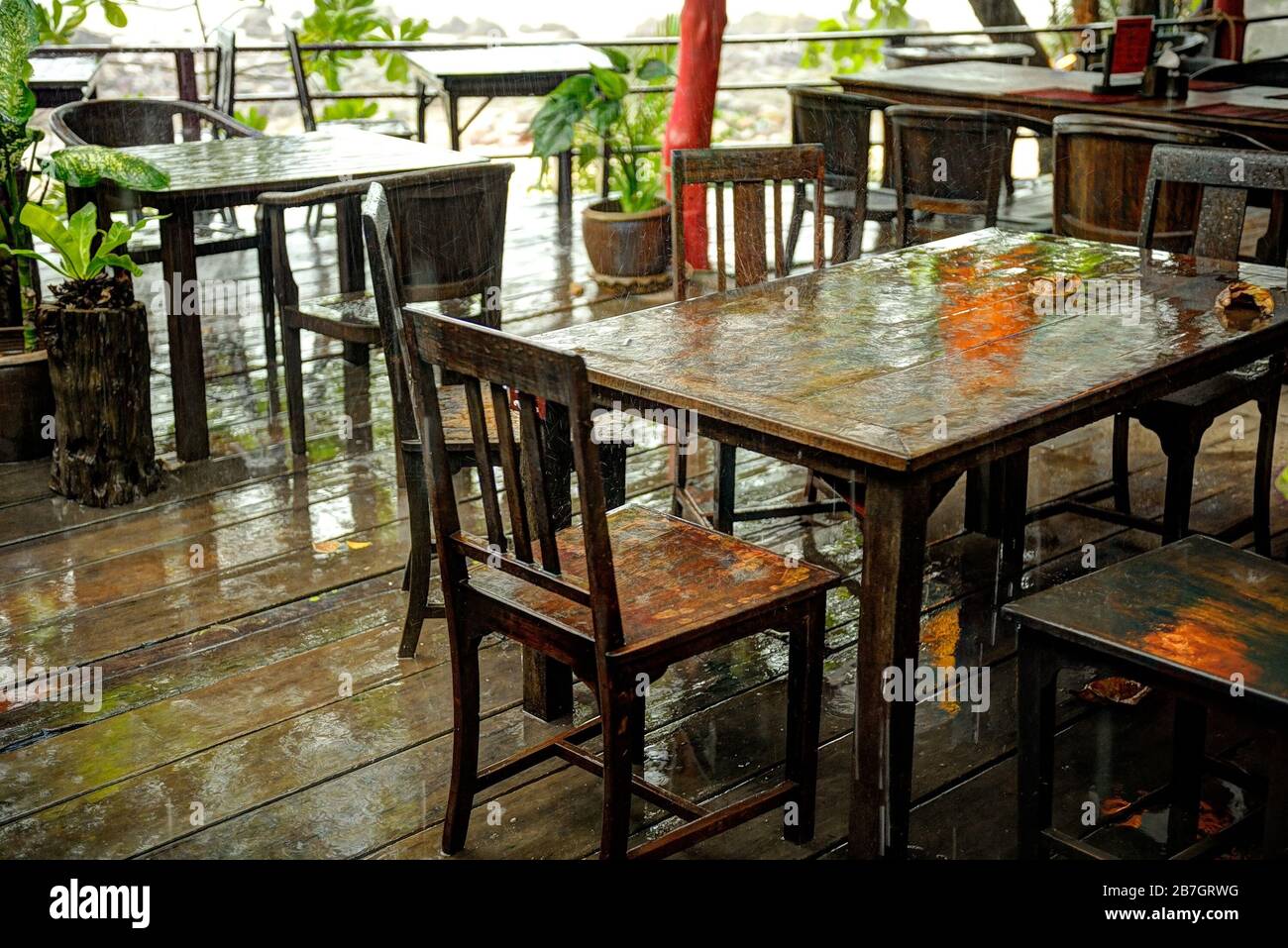 Wooden tables and chairs under heavy rain in outdoor beach restaurant ...