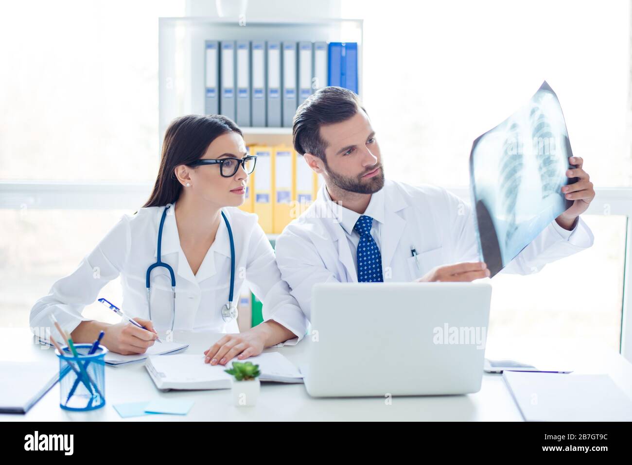 Two serious confident doctors checking the x-ray of their patient and ...