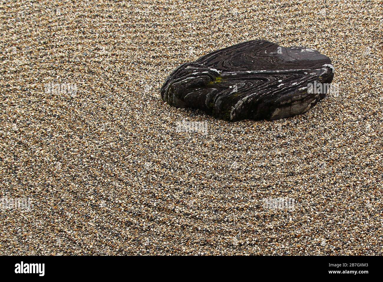 Zen stone in wavy raked gravel Stock Photo - Alamy
