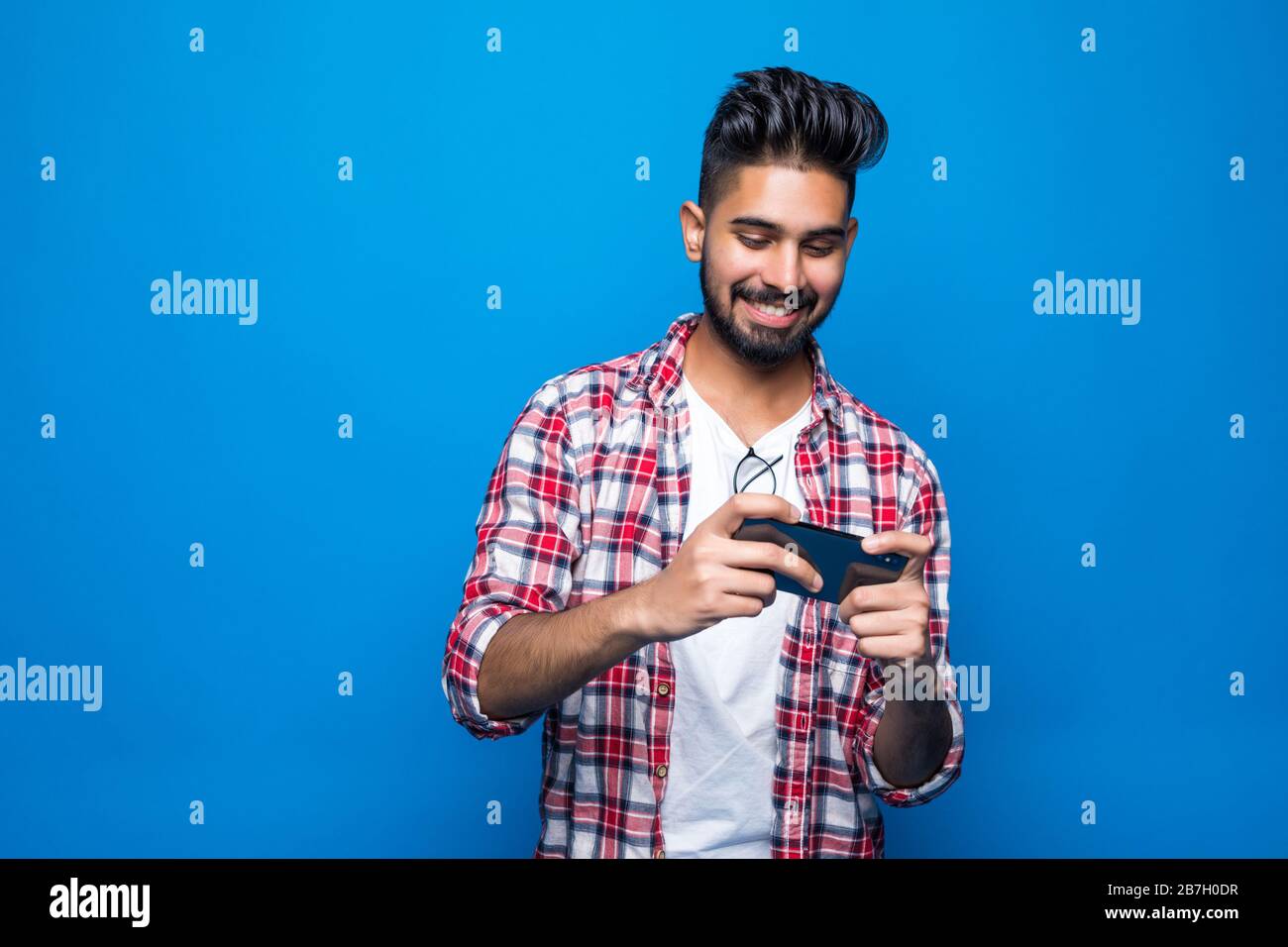 Young happy bearded indian man play games on mobile phone posing over ...