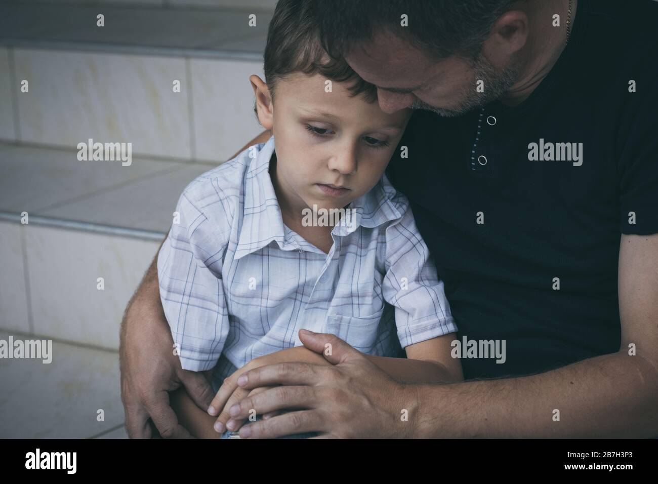 Portrait of young sad little boy and father sitting outdoors at the day ...
