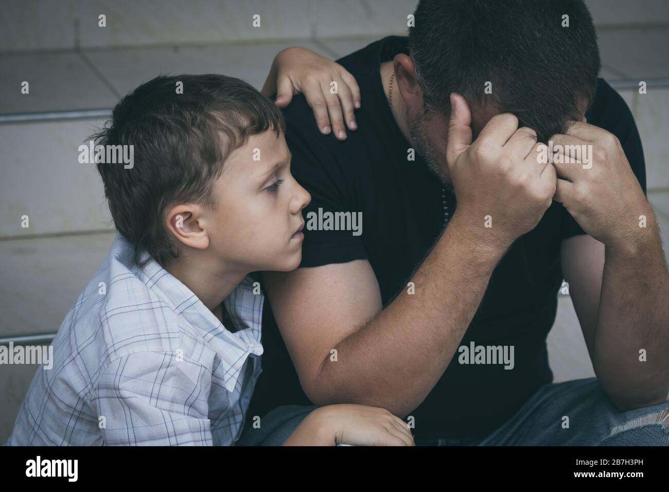 Portrait of young sad little boy and father sitting outdoors at the day ...