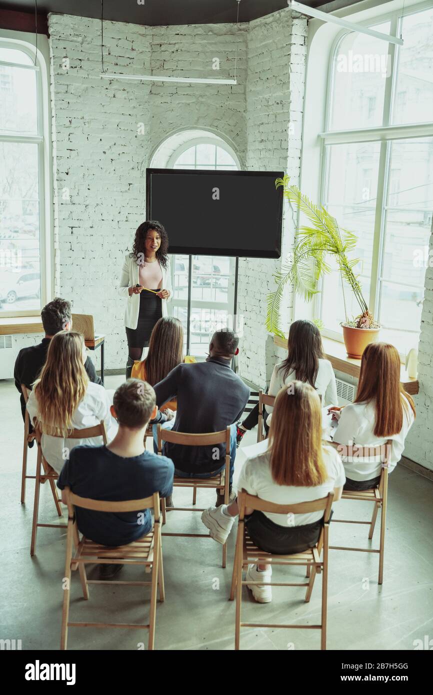Female african-american speaker giving presentation in hall at workshop. Audience or hall. Rear ...