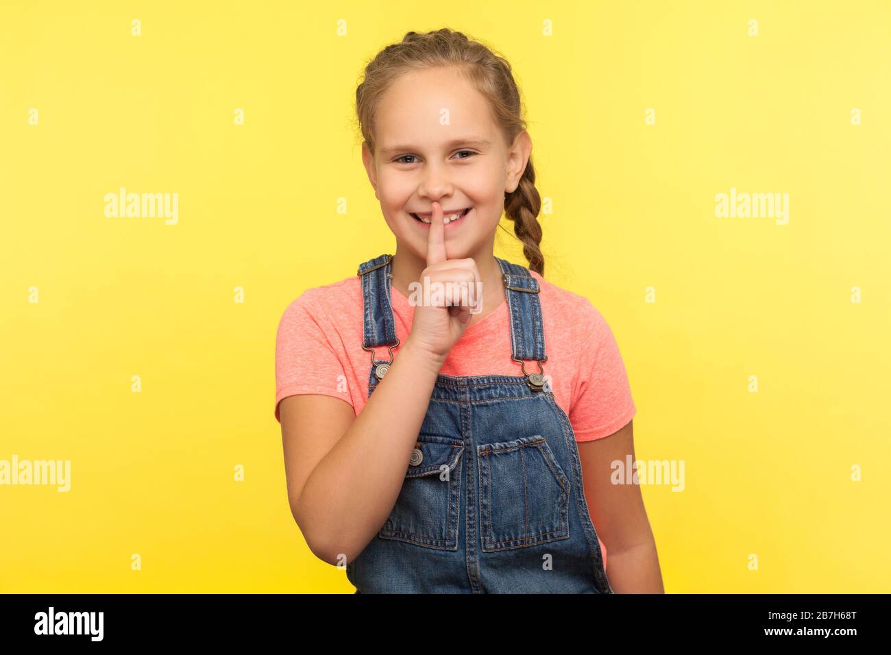 Be quiet, it's secret. Portrait of positive little girl with braid in ...