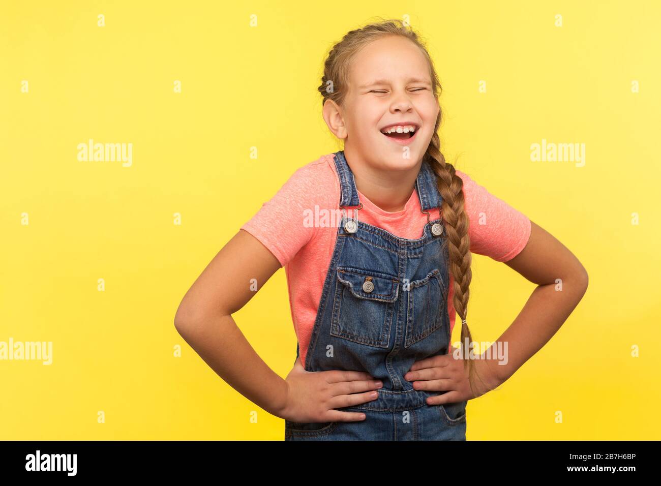 Portrait of unhealthy child with braid in denim overalls clutching ...