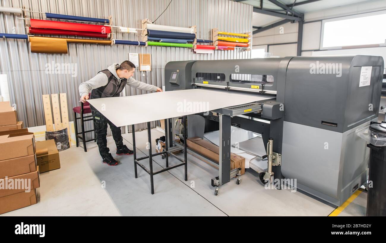 Technician worker operator works on large premium industrial printer ...