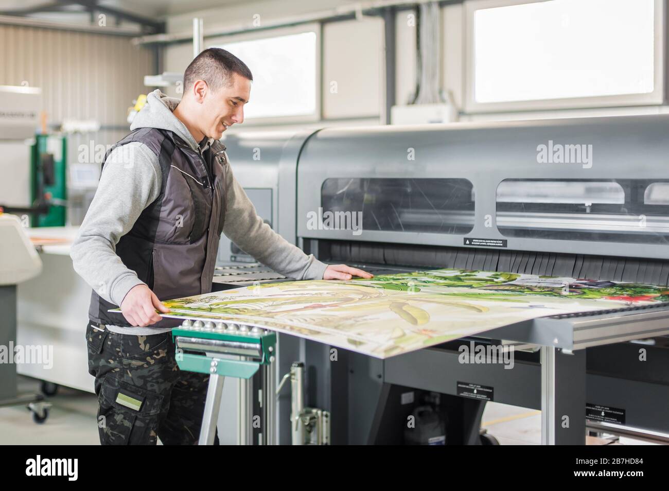 Technician worker operator works on large premium industrial printer and plotter machine in ...
