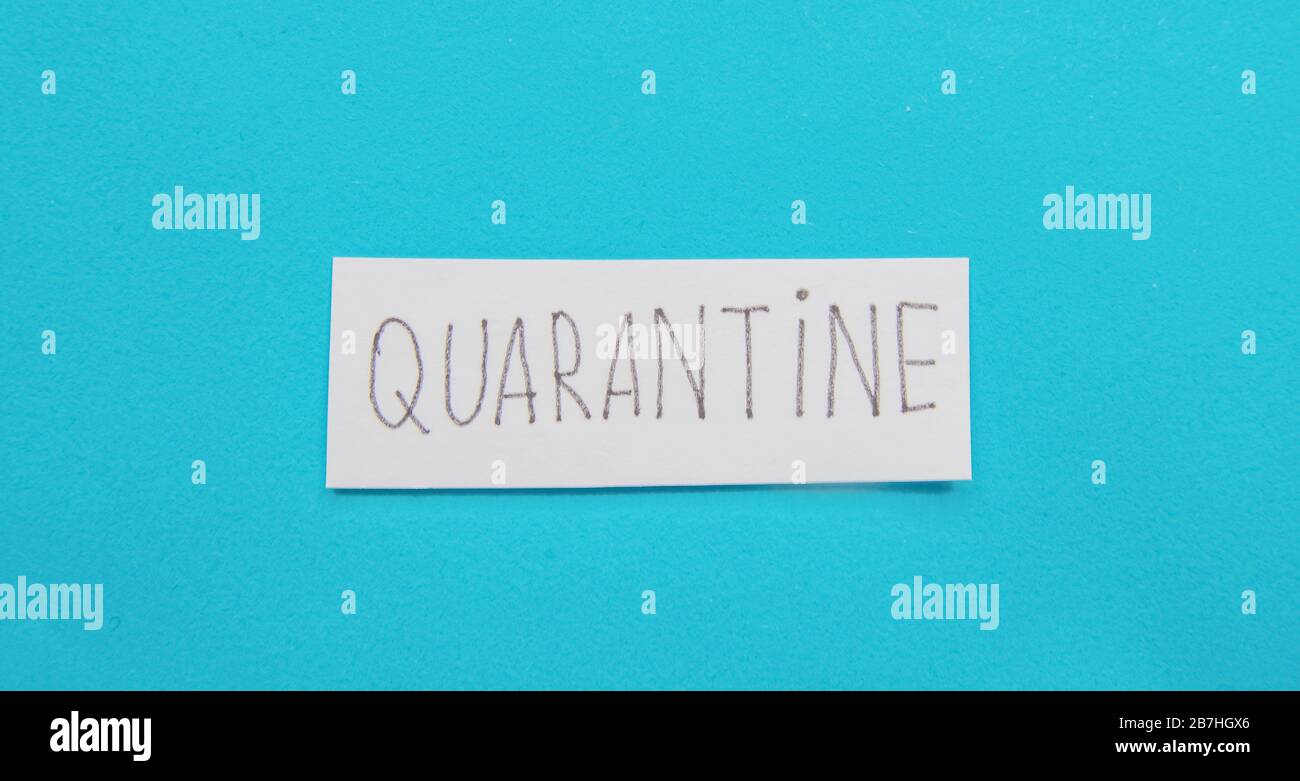 The word quarantine written on a piece of paper, top view on a blue ...