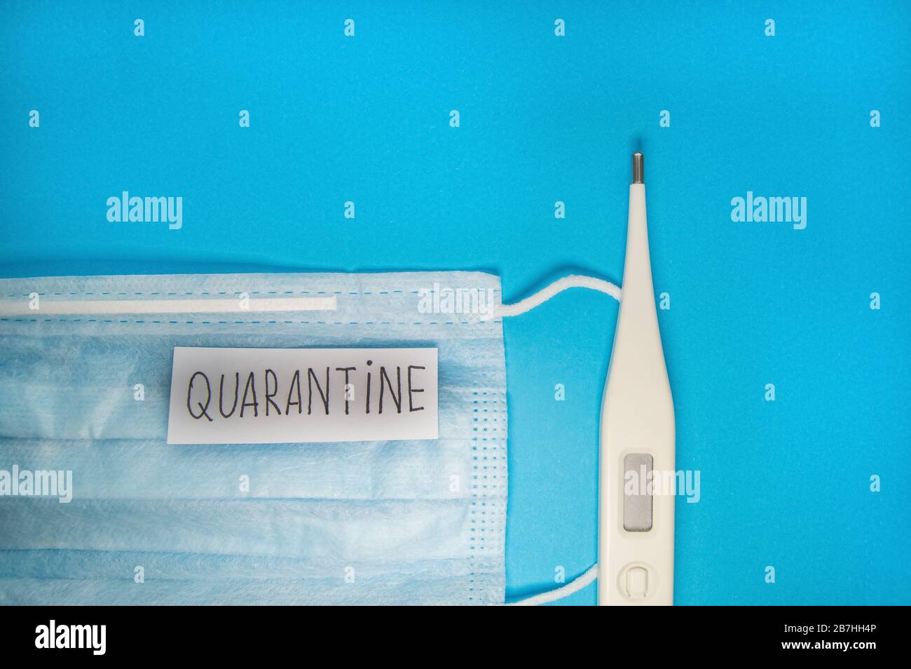 Medical mask, thermometer and text QUARANTINE on a blue background, top ...