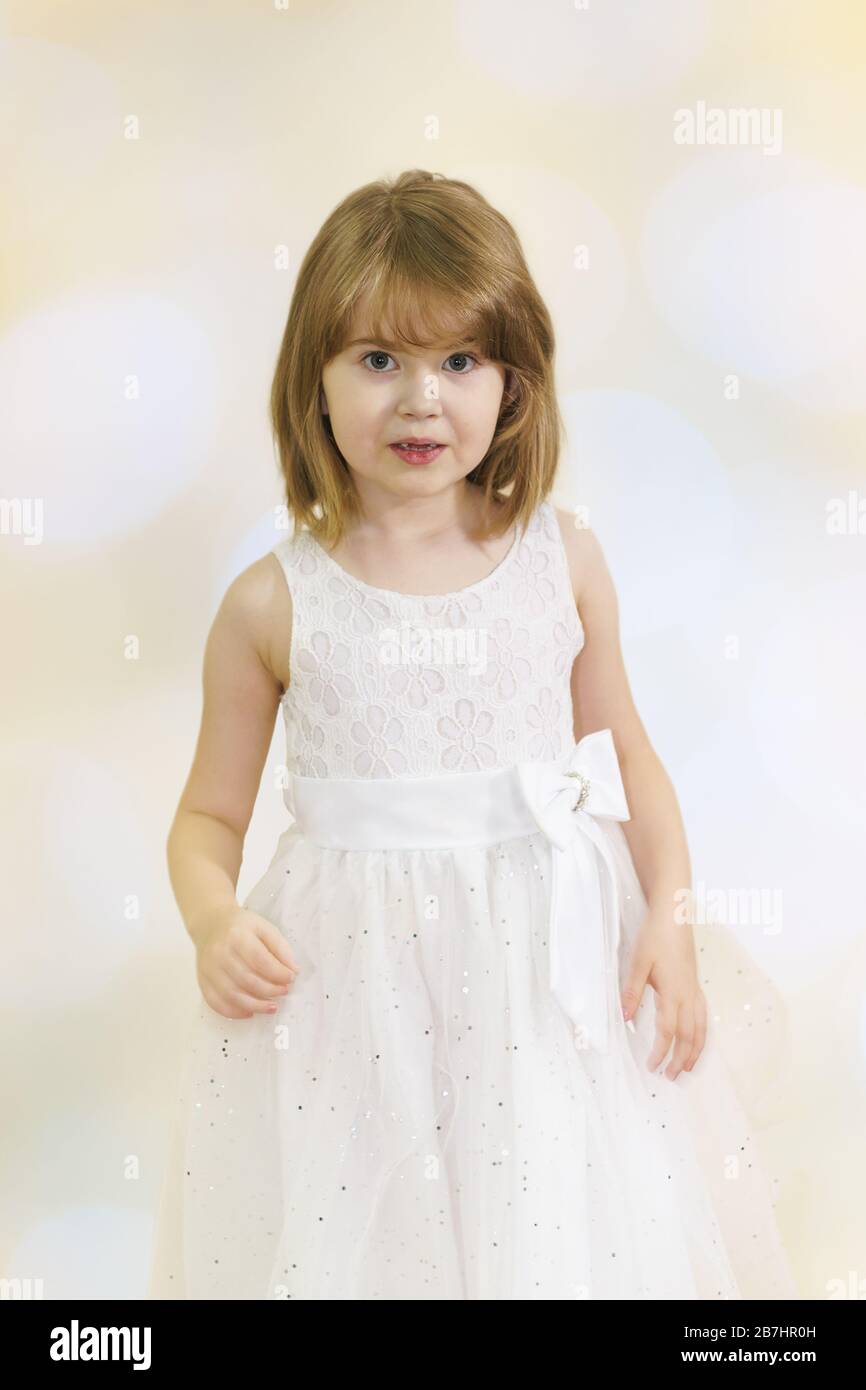 Beautiful surprised toothless little girl in white dress. Sunny yellow ...