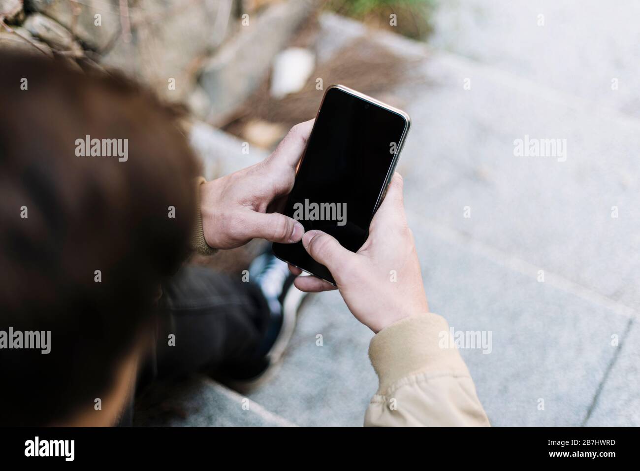Rear view of a hispanic young man using mobile phone while sitting ...