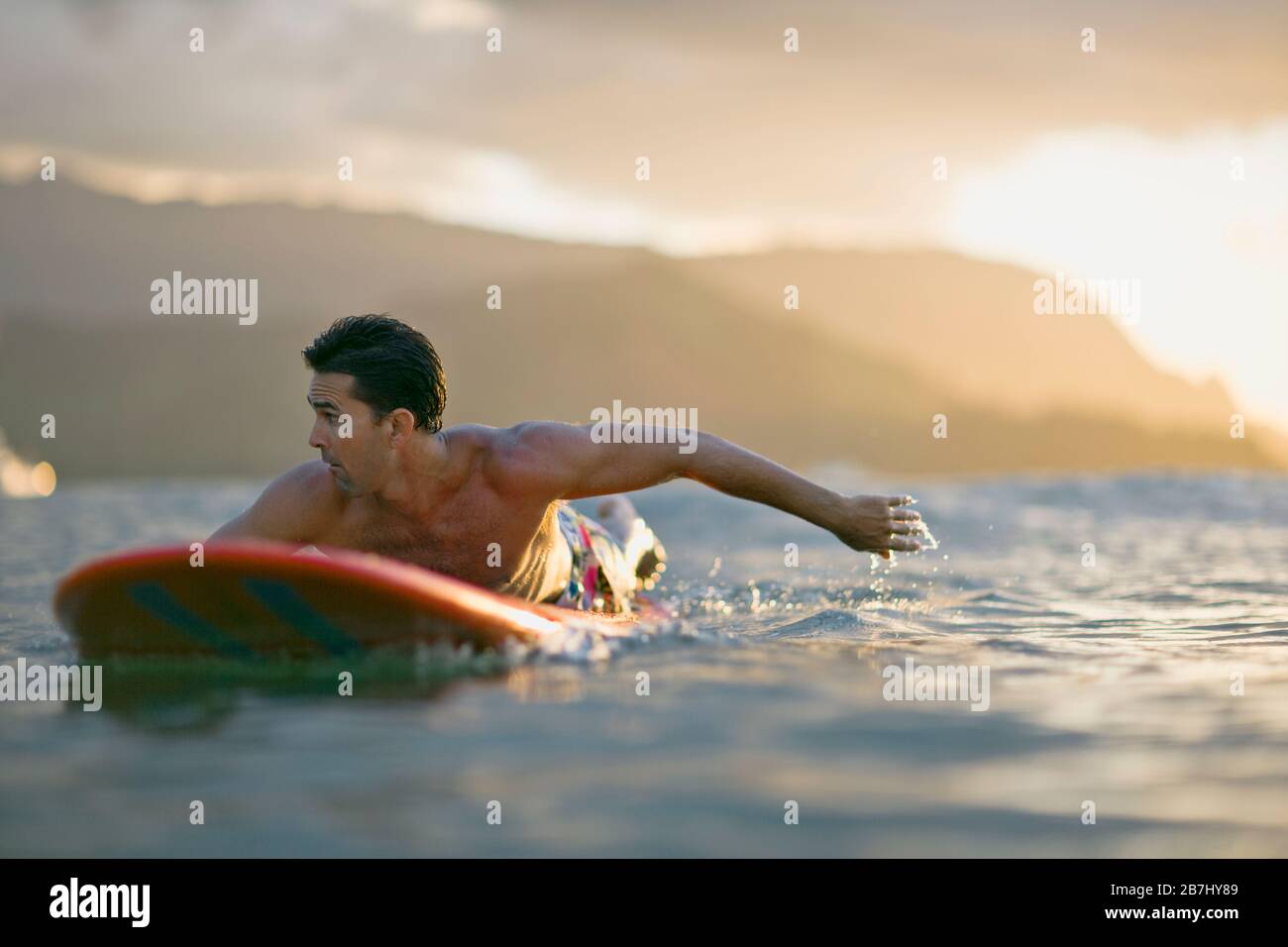 Male surfer lies on his board, looks over his shoulder and paddles in ...