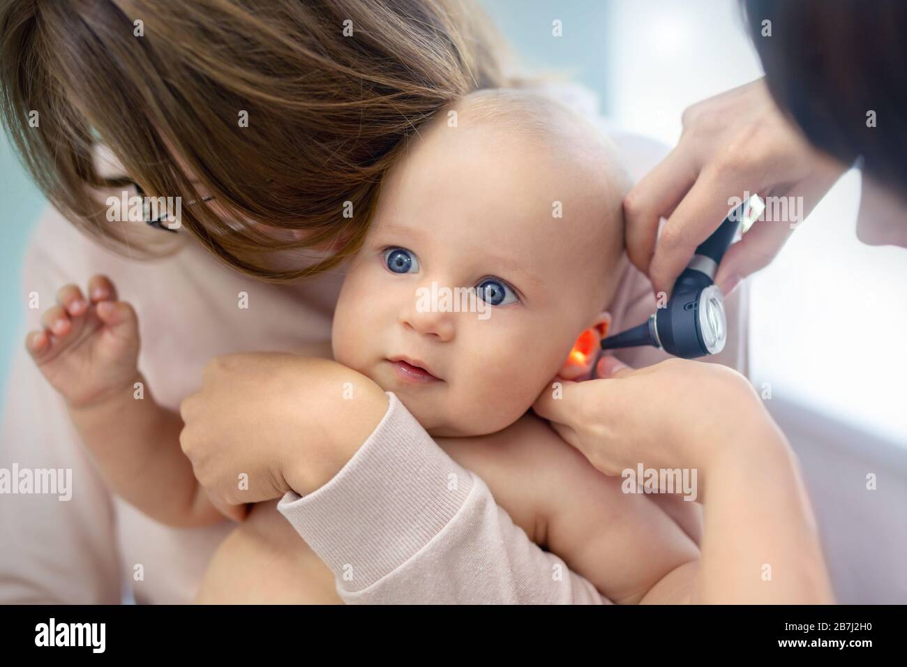 Doctor pediatrist examining childs ear with otoscope. Mom holding baby ...