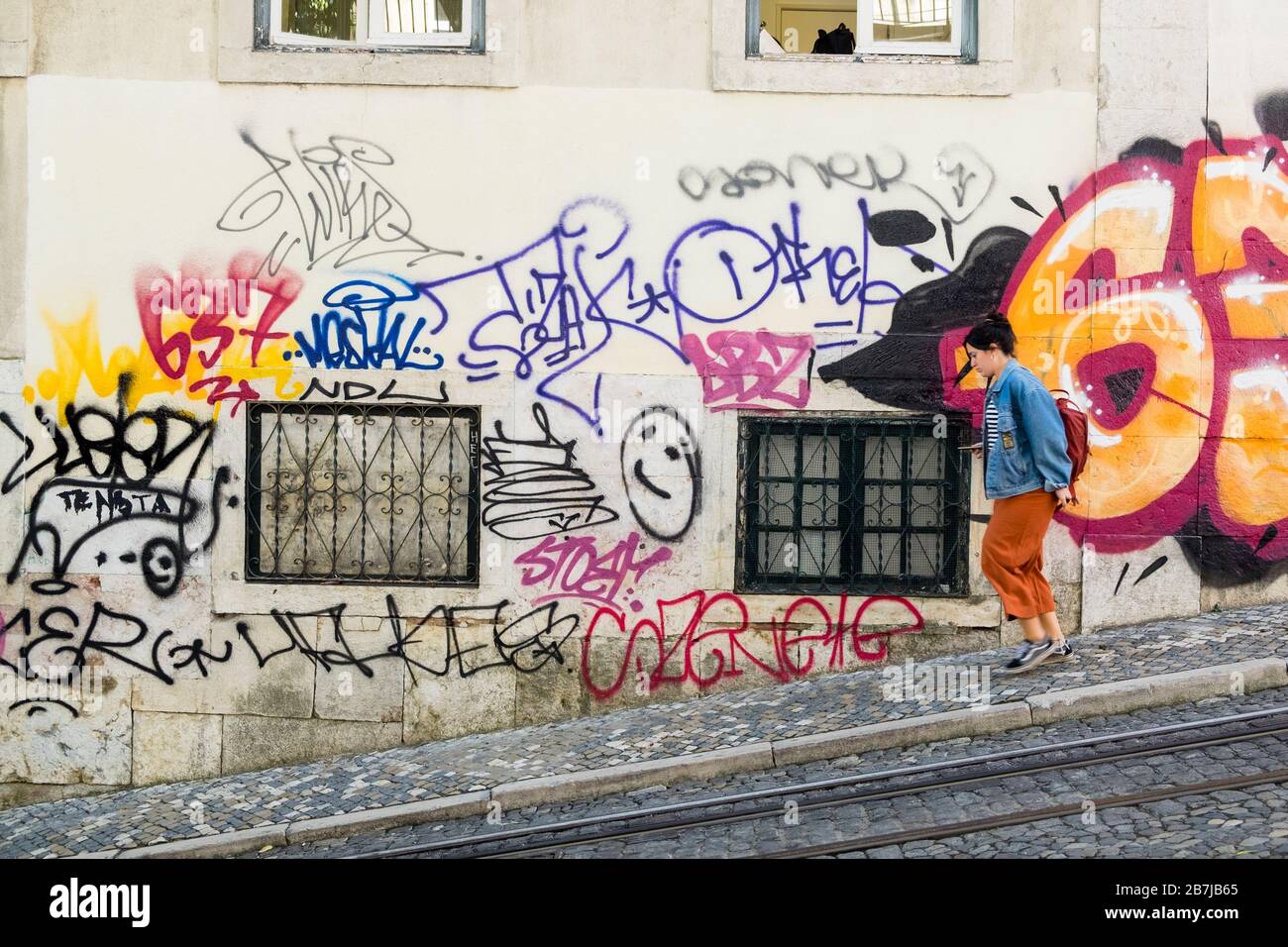Woman walking down steep cobblestone sidewalk in Lisbon, with graffiti ...