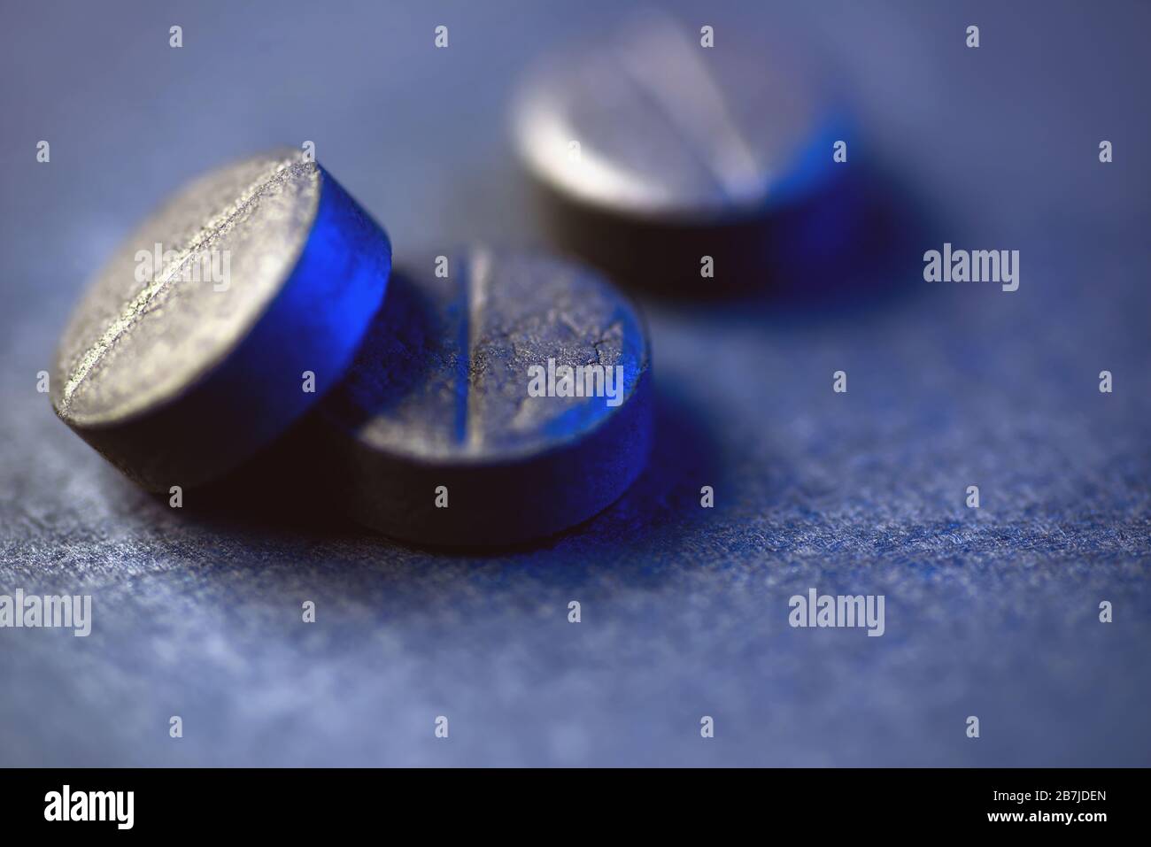 Three black activated charcoal tablets. On a black background. There's ...