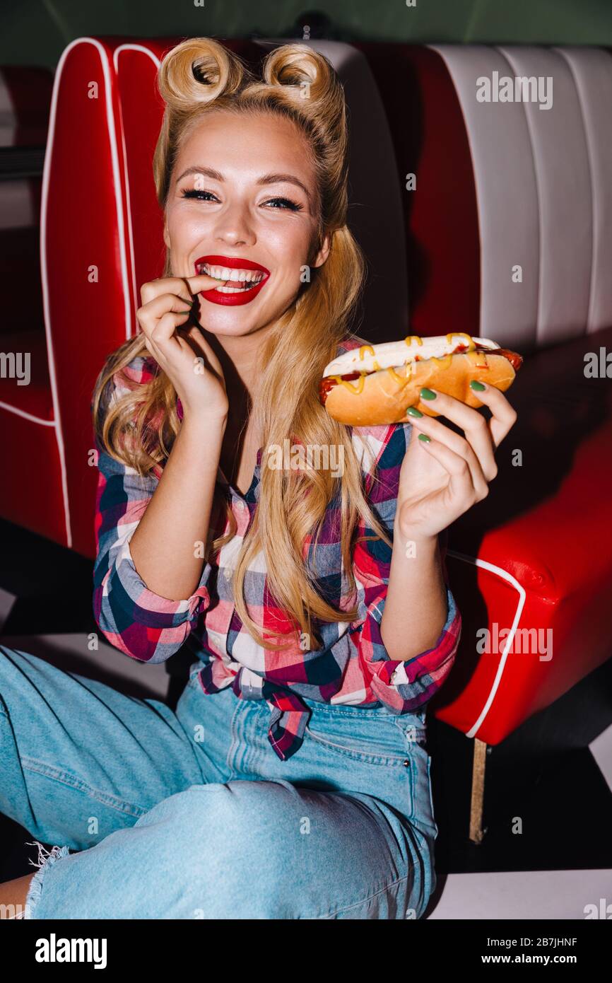Photo of young laughing woman with beautiful hairstyle eating hotdog ...
