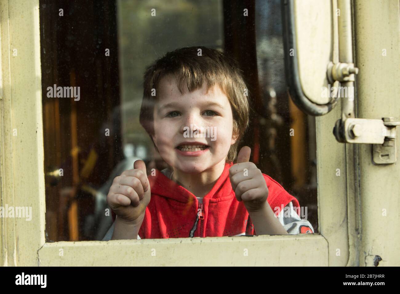 Young hapy caucasian boy doing thumbs up gesture through a train door ...