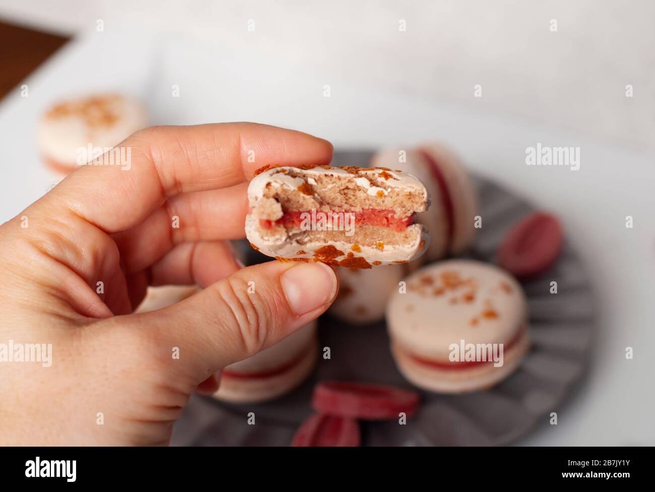 Hand holds a bitten strawberry macaron Stock Photo - Alamy