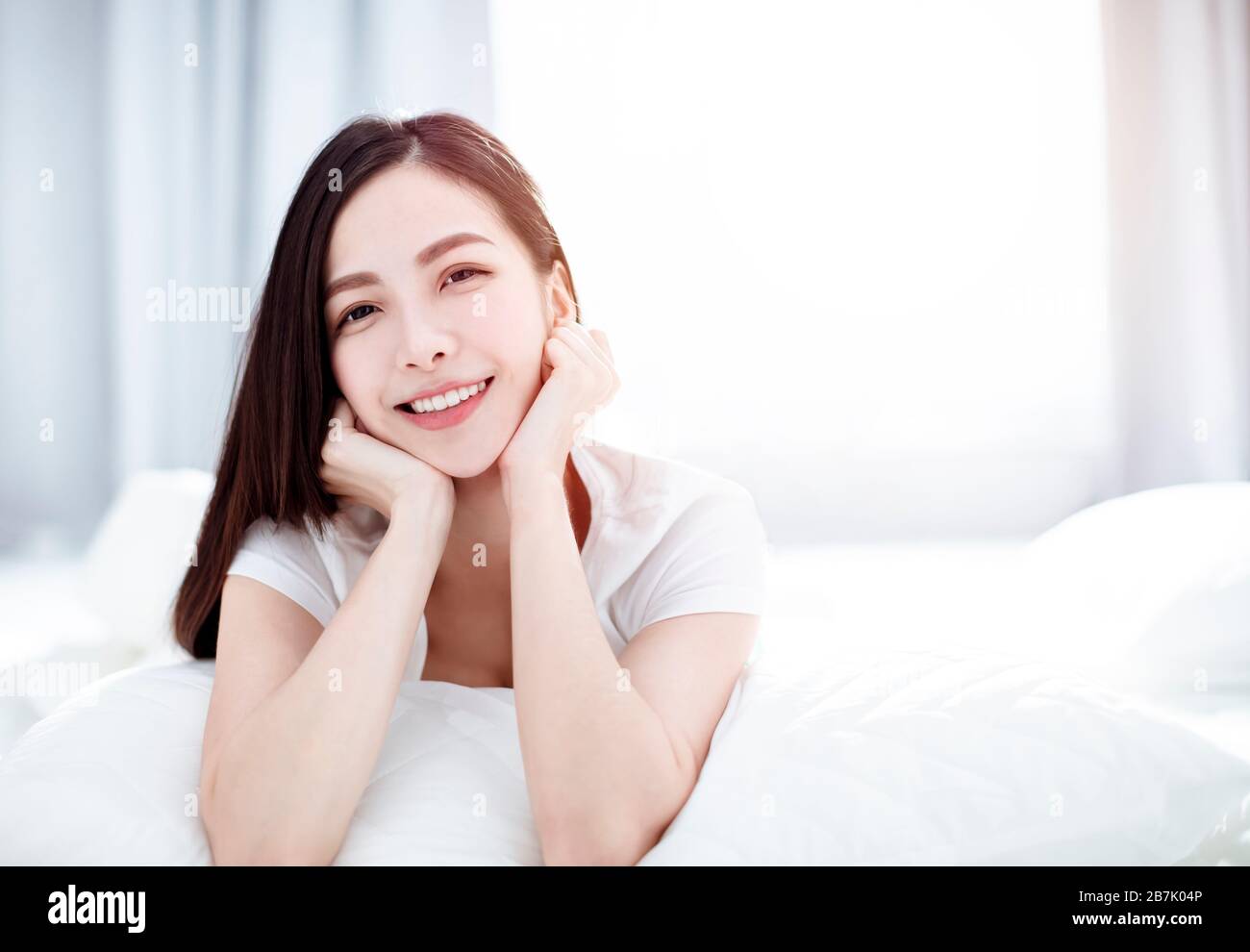 Young smiling woman lying in bed in bedroom Stock Photo - Alamy