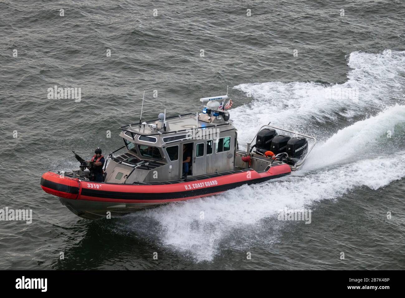 Coast Guard member stands ready with gun on US Coast Guard boat as it ...