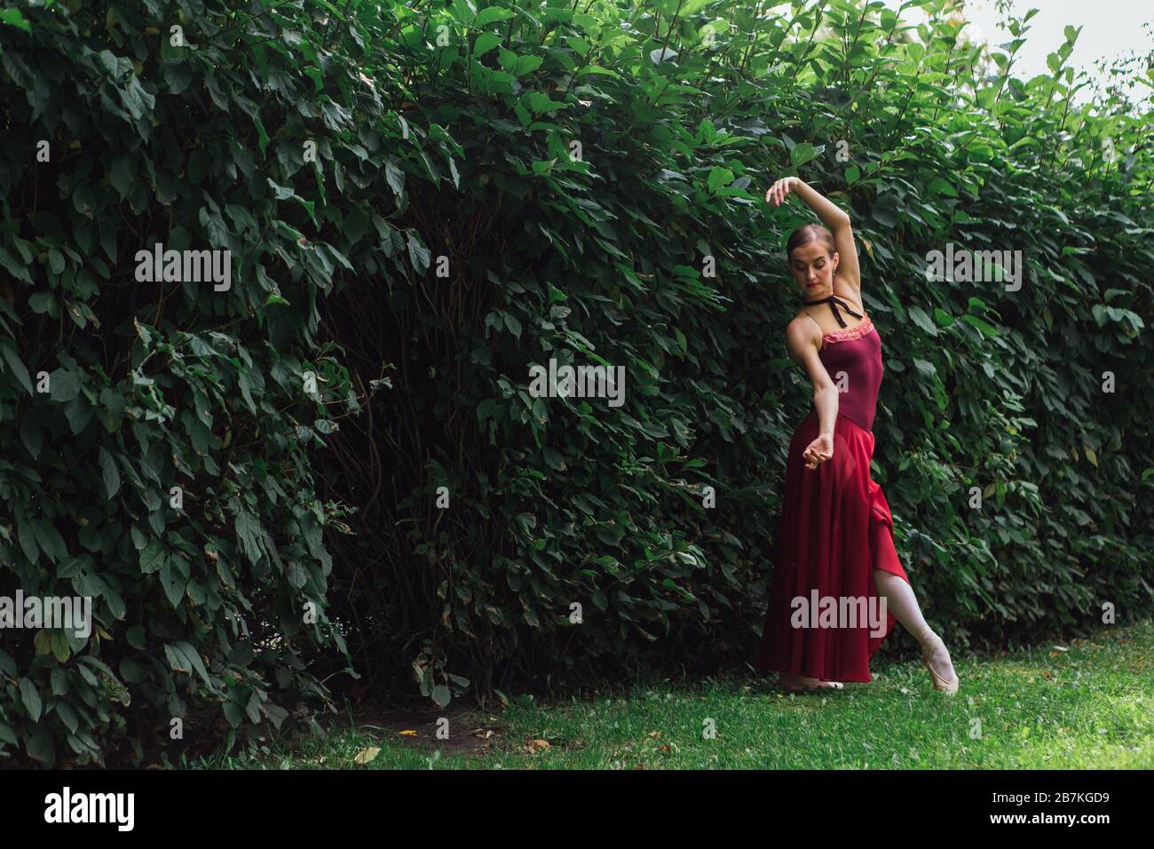 Woman ballerina in red ballet dress dancing in pointe shoes posing next ...