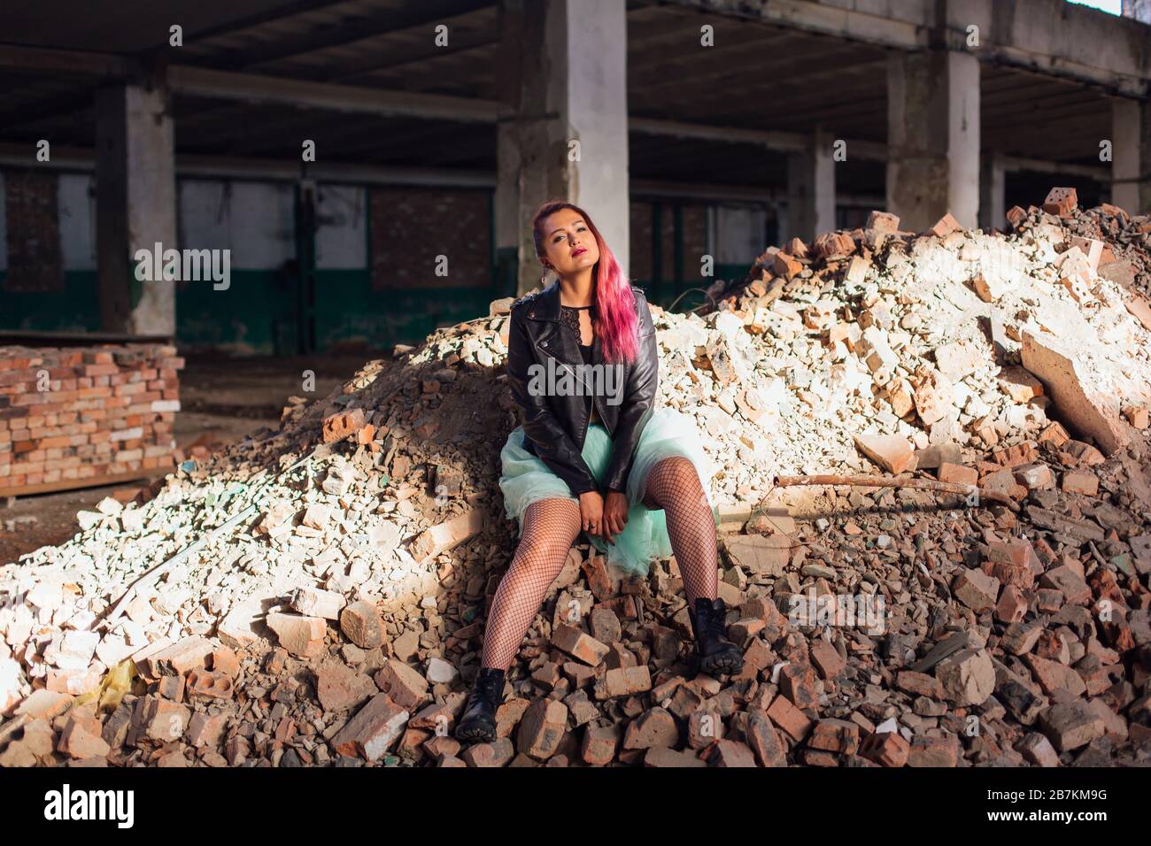 Young girl with pink hair sitting on bricks in a collapsed building ...