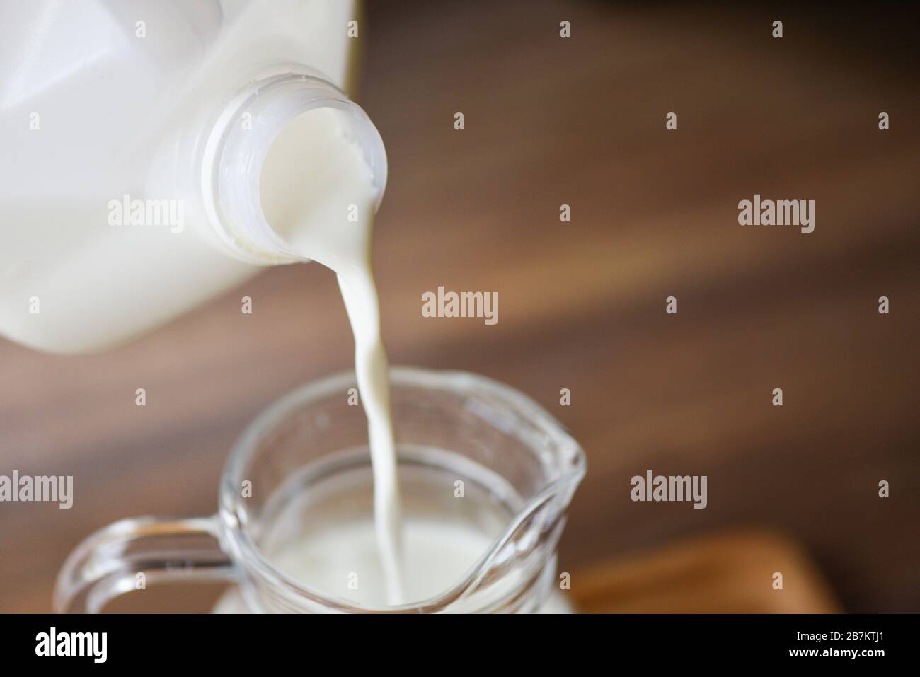 Fresh milk natural in bottle and Pouring milk into glass jug on wooden ...