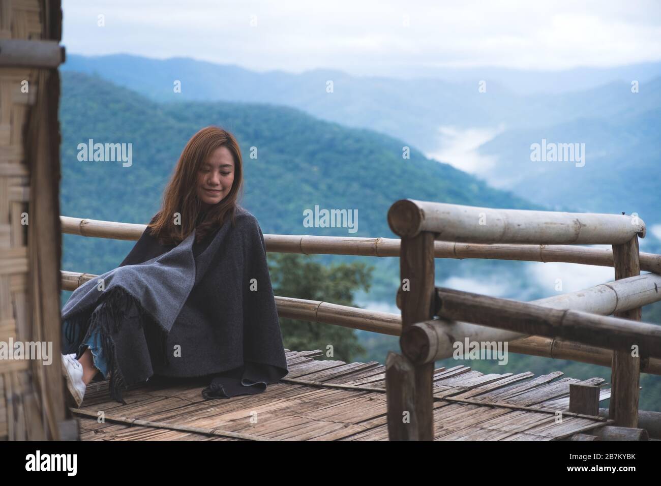 A beautiful asian woman sitting alone on wooden balcony with mountains view on foggy day and ...