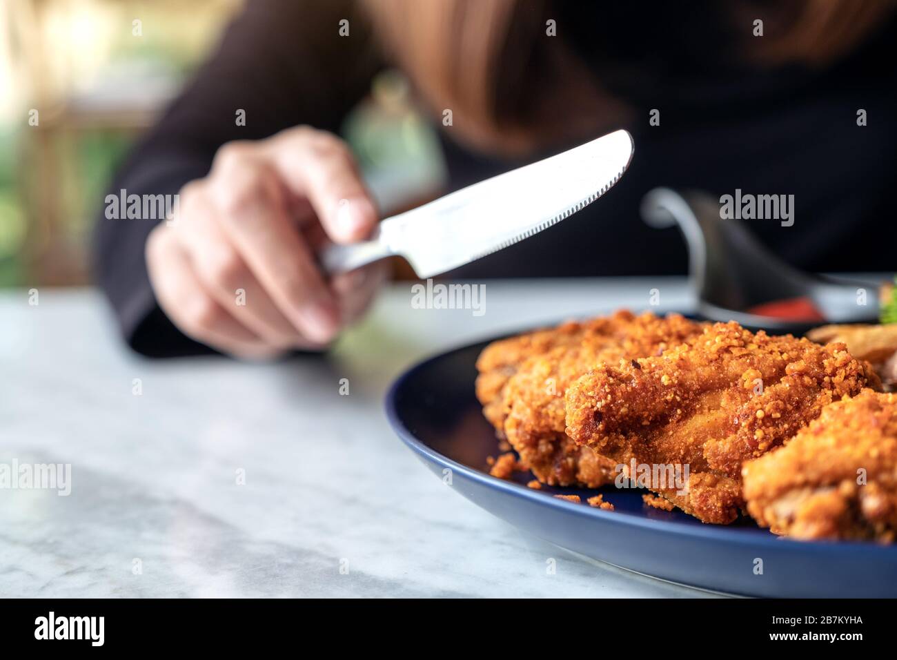 Closeup image of a woman's hand using knife to eat fried chicken and ...