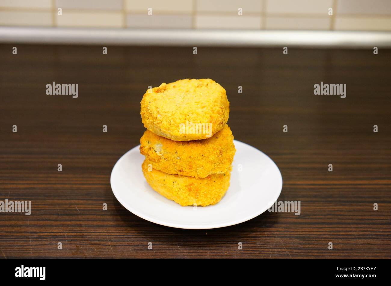 Closeup shot of breaded fish burgers stack on white plate on a wooden ...