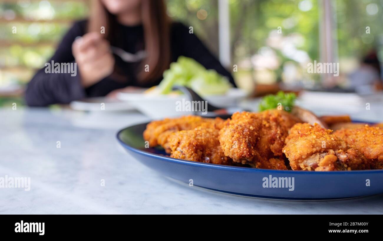 Closeup image of a plate of fried chicken and french fries with a woman ...