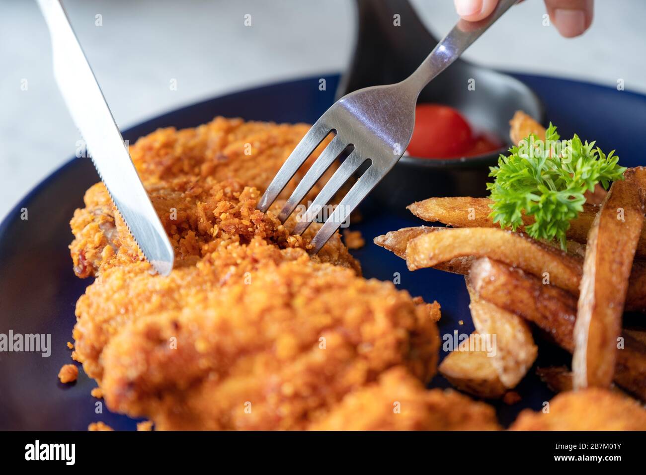 Closeup image of a person using knife and fork to eat fried chicken and ...