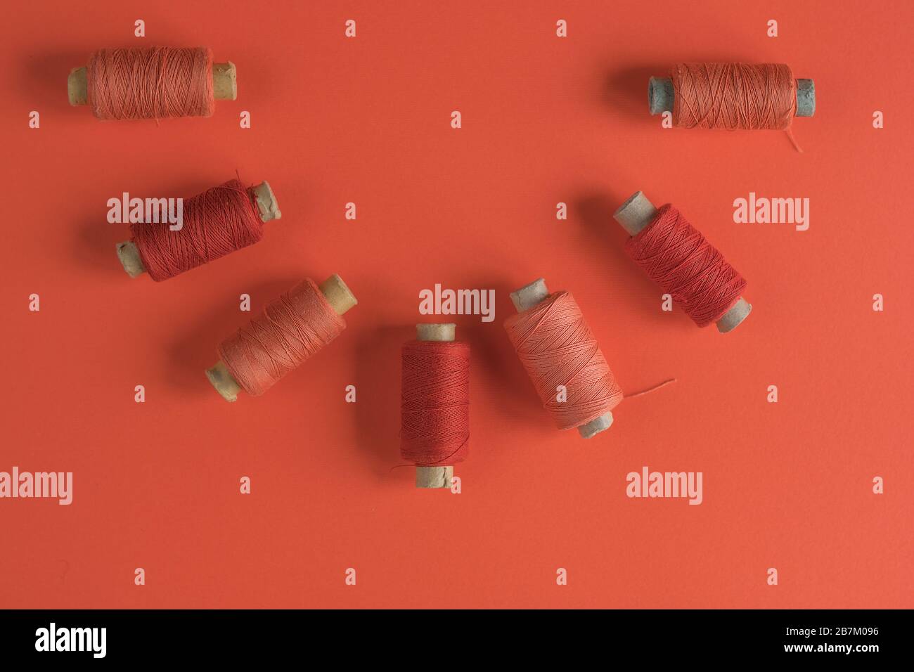 A coral spool of threads on coral paper background, with copy space ...