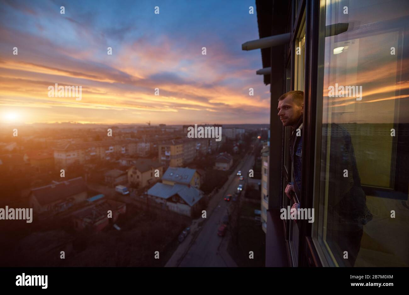 Side view of a smiling man looking away from a balcony at sunset ...