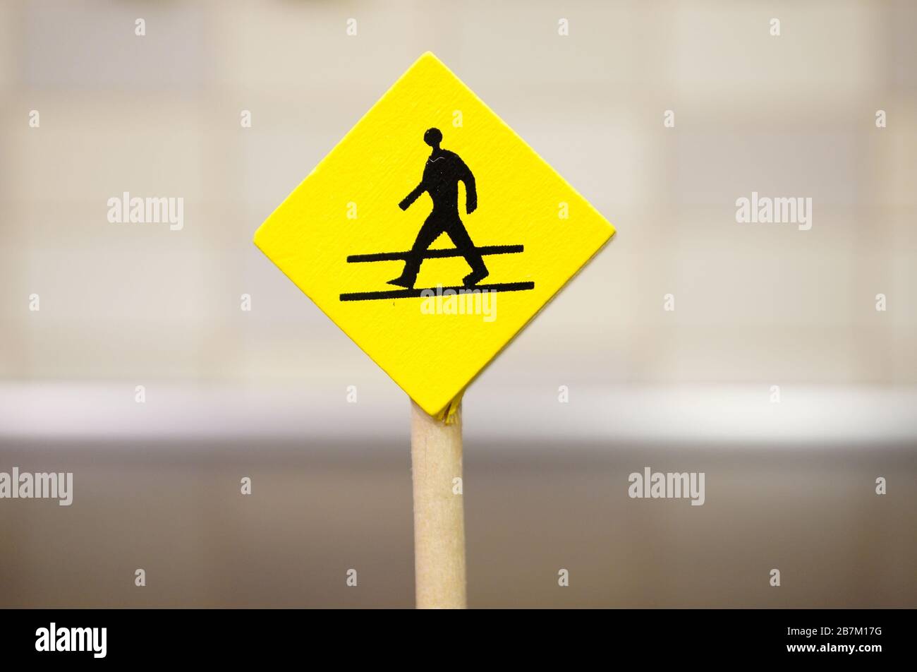 Yellow wooden toy sign with a walking person icon on a blurred ...