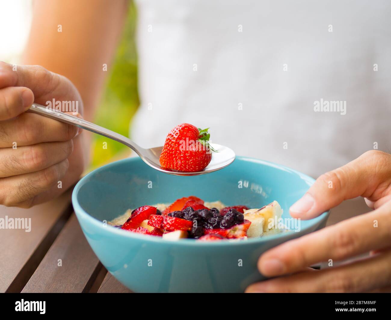 Heart shape strawberry in man hands on a white shirt background ...