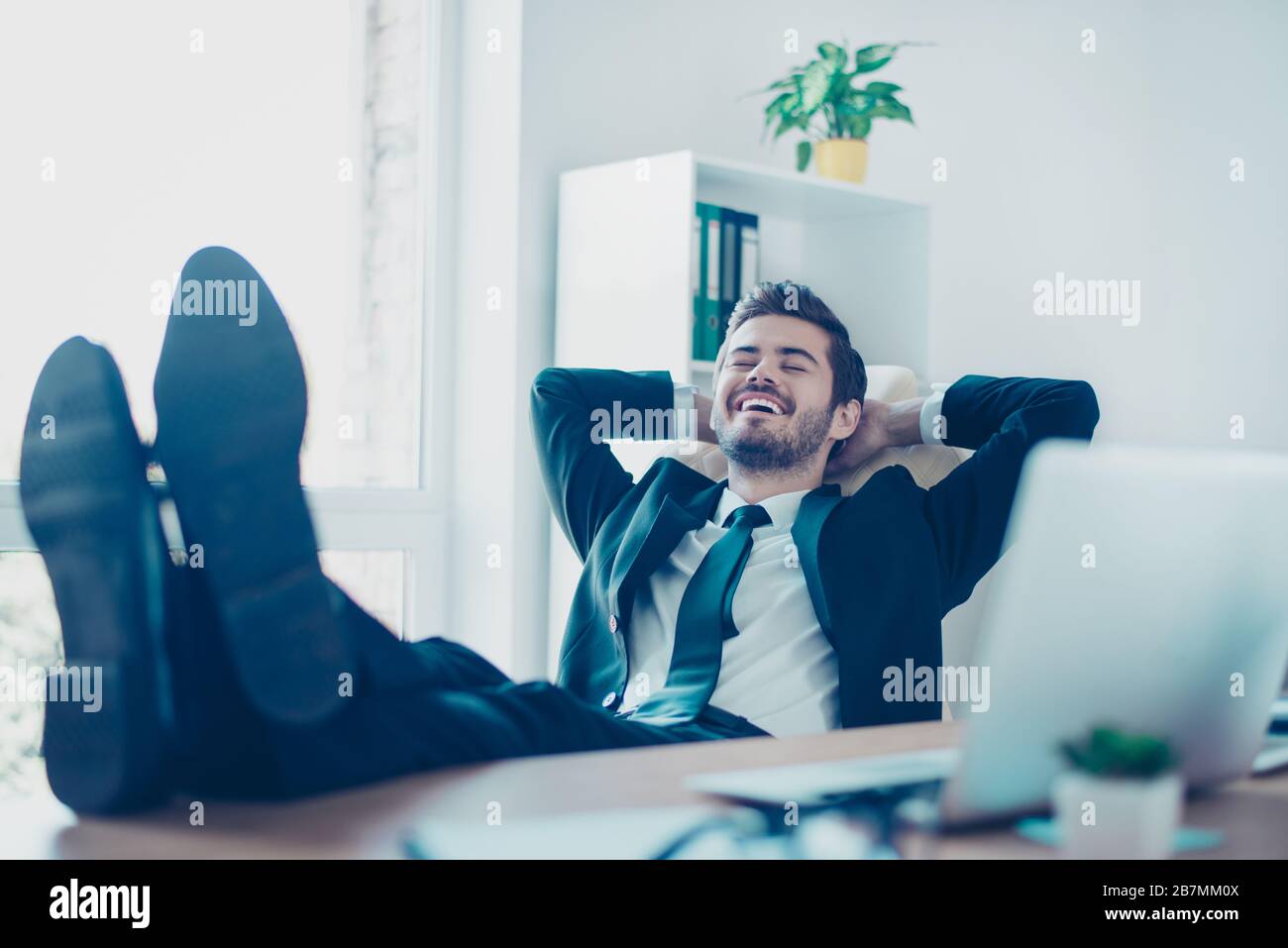 Happy cheerful smiling young entrepreneur lying on the chair with legs ...