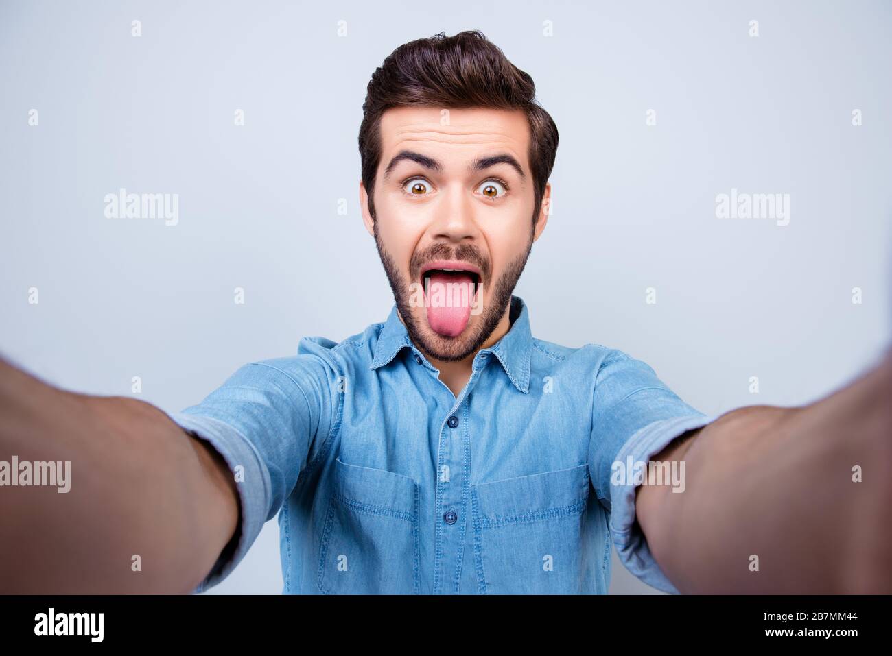 Playful stylish man on light blue background is showing his tongue and ...