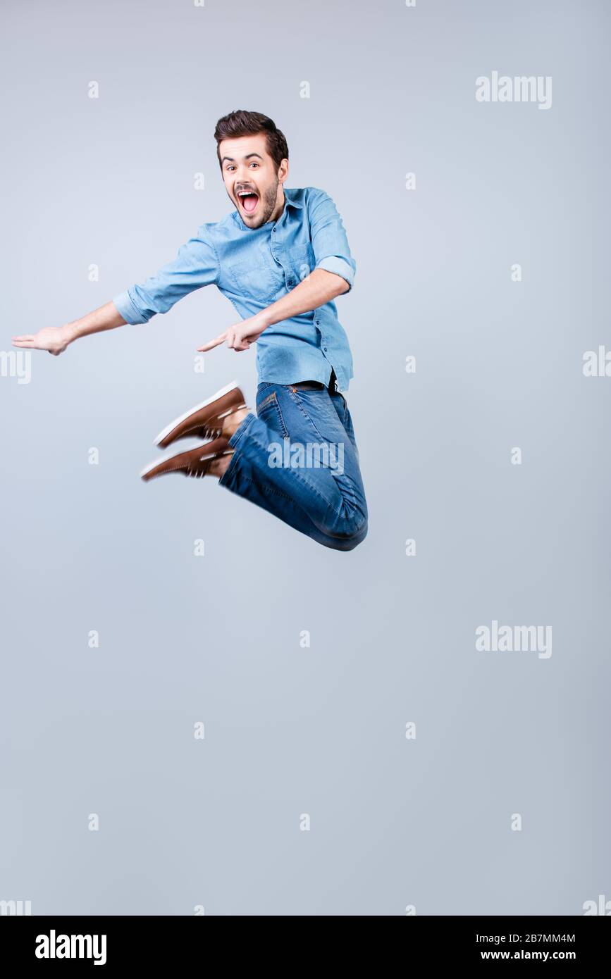 Happy young guy is jumping and pointing on his right. He is in casual ...