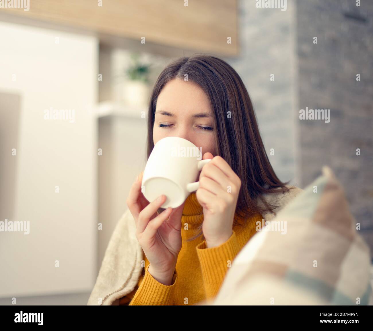 Ill young woman with flu virus at home drinking tea covered in blanket ...