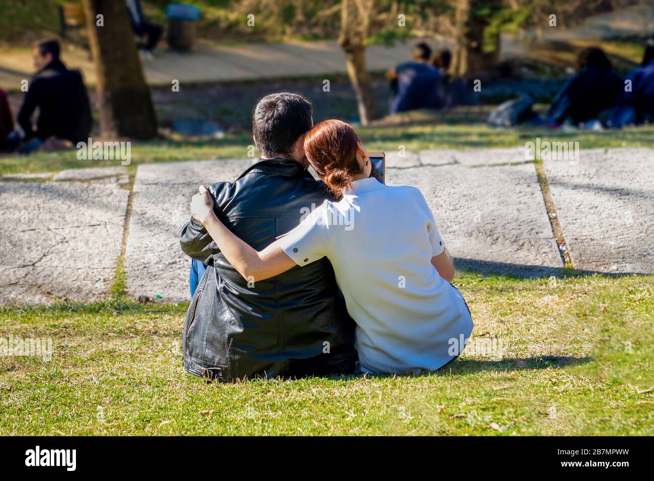 Back view of woman's arm on man's shoulder and they are sitting and ...