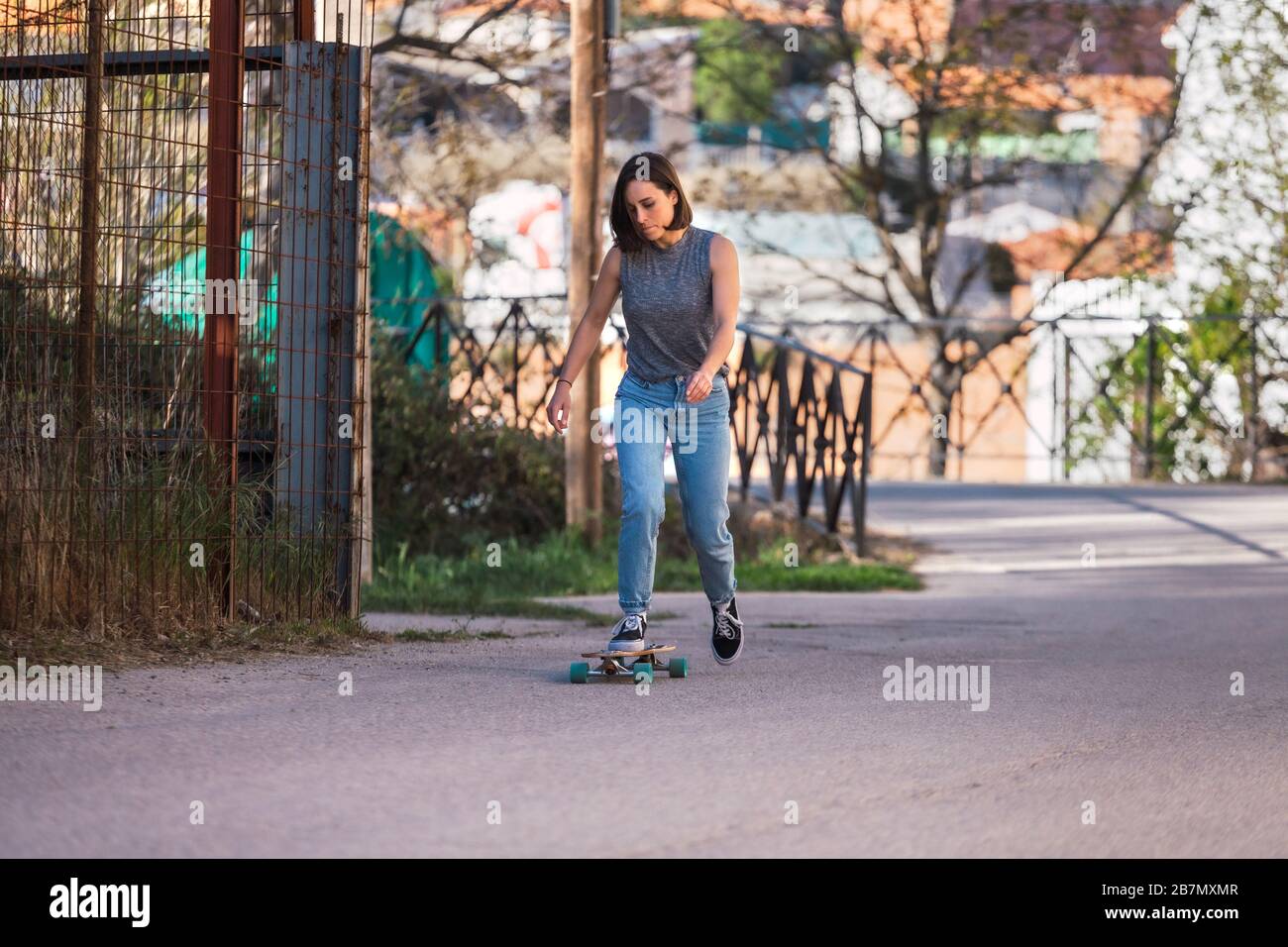 Young skater woman riding on her longboard in the village in casual ...
