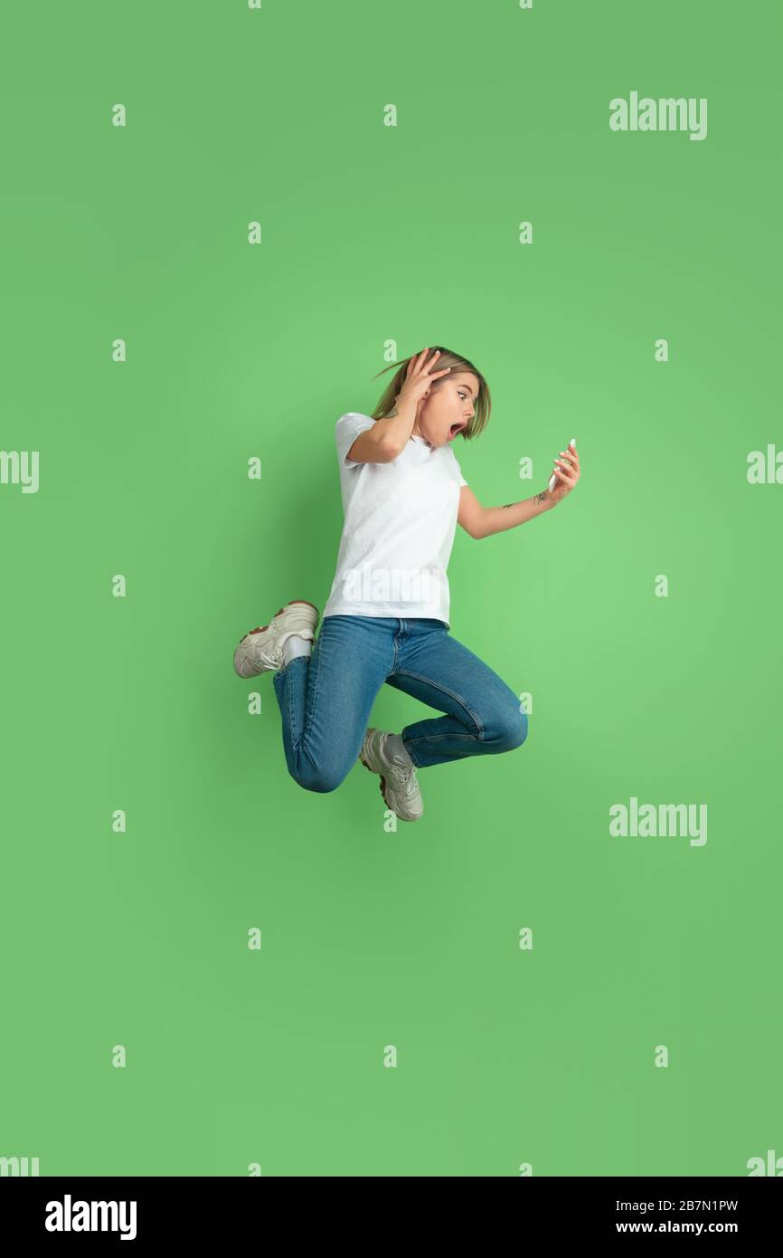 Shocked using phone in jump. Caucasian young woman's portrait isolated ...