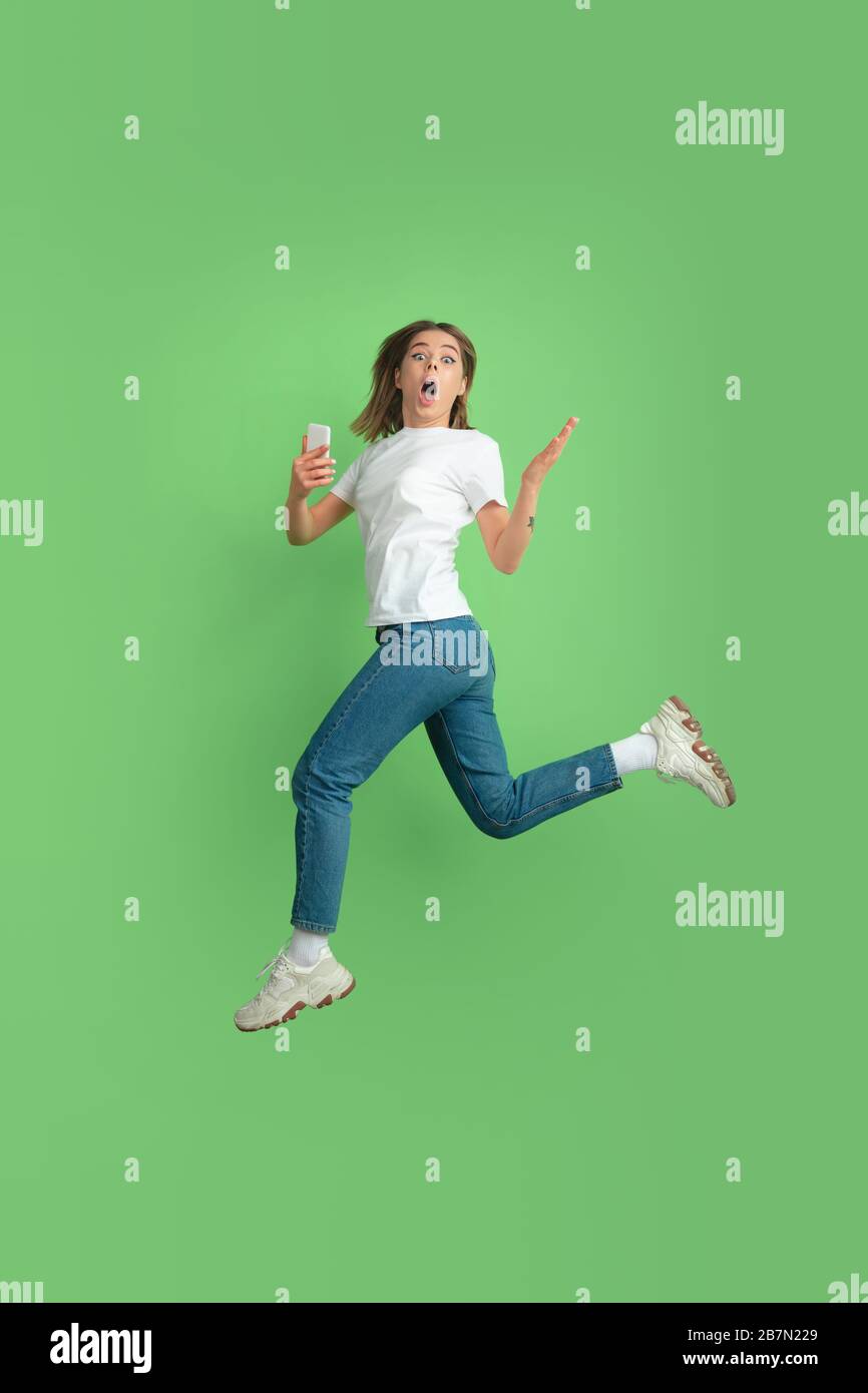 Shocked using phone in jump. Caucasian young woman's portrait isolated ...